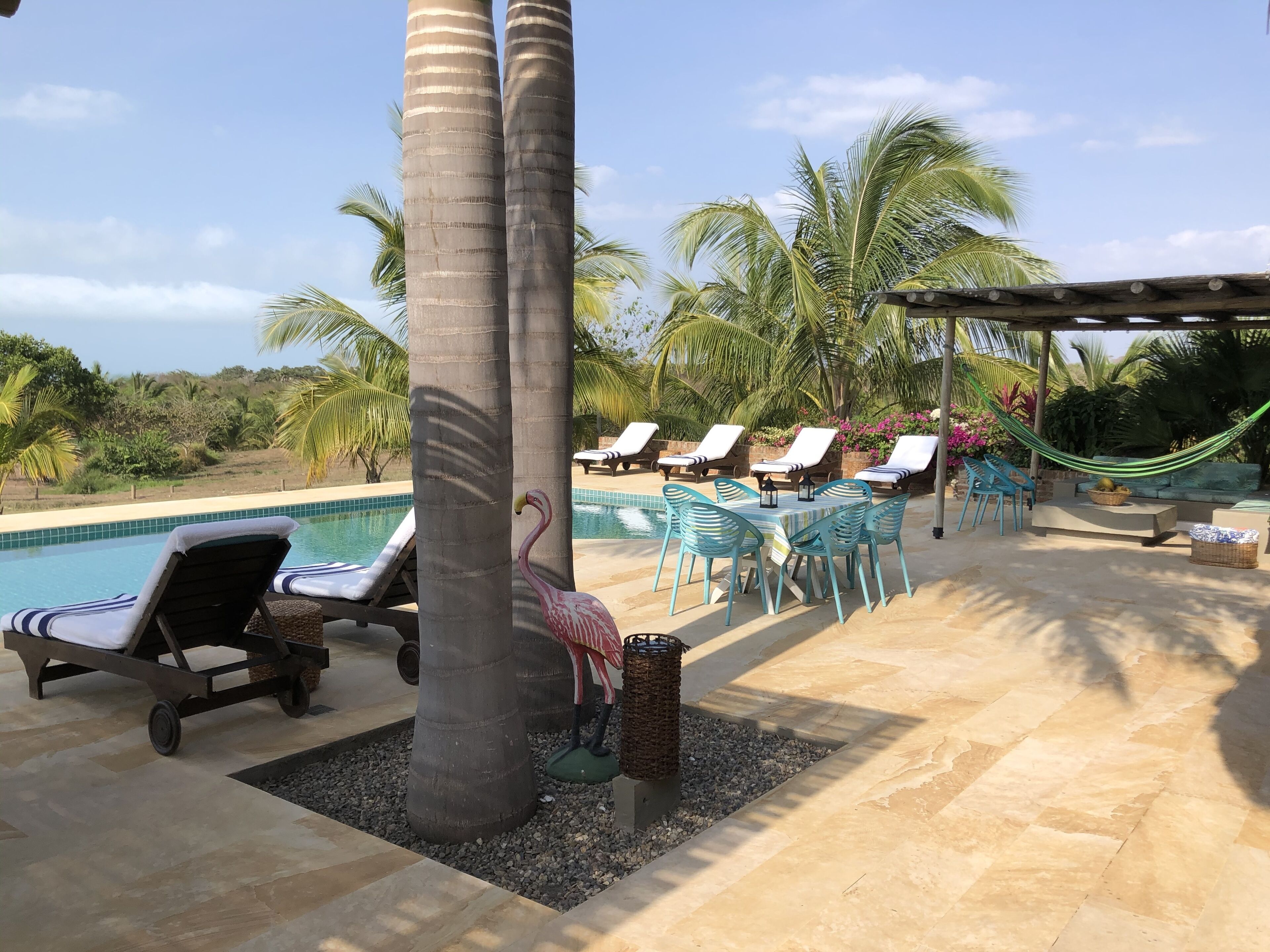 Uma área à beira da piscina com espreguiçadeiras, mesa de jantar e rede.