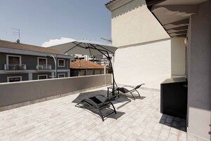 Terraço no telhado com pérgola, duas cadeiras de descanso e churrasqueira.