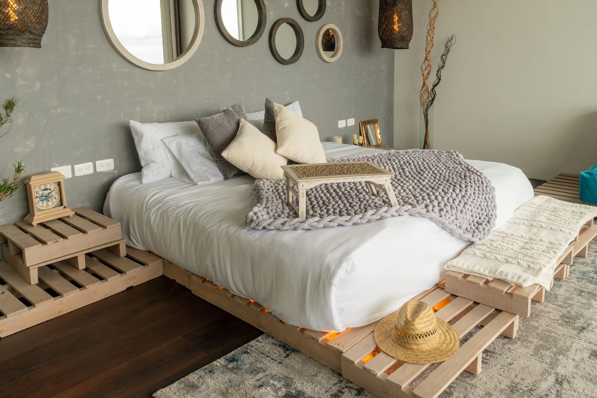 Um quarto moderno com uma cama plataforma de madeira, um cobertor de tricô cinza e um cesto trançado na cama.