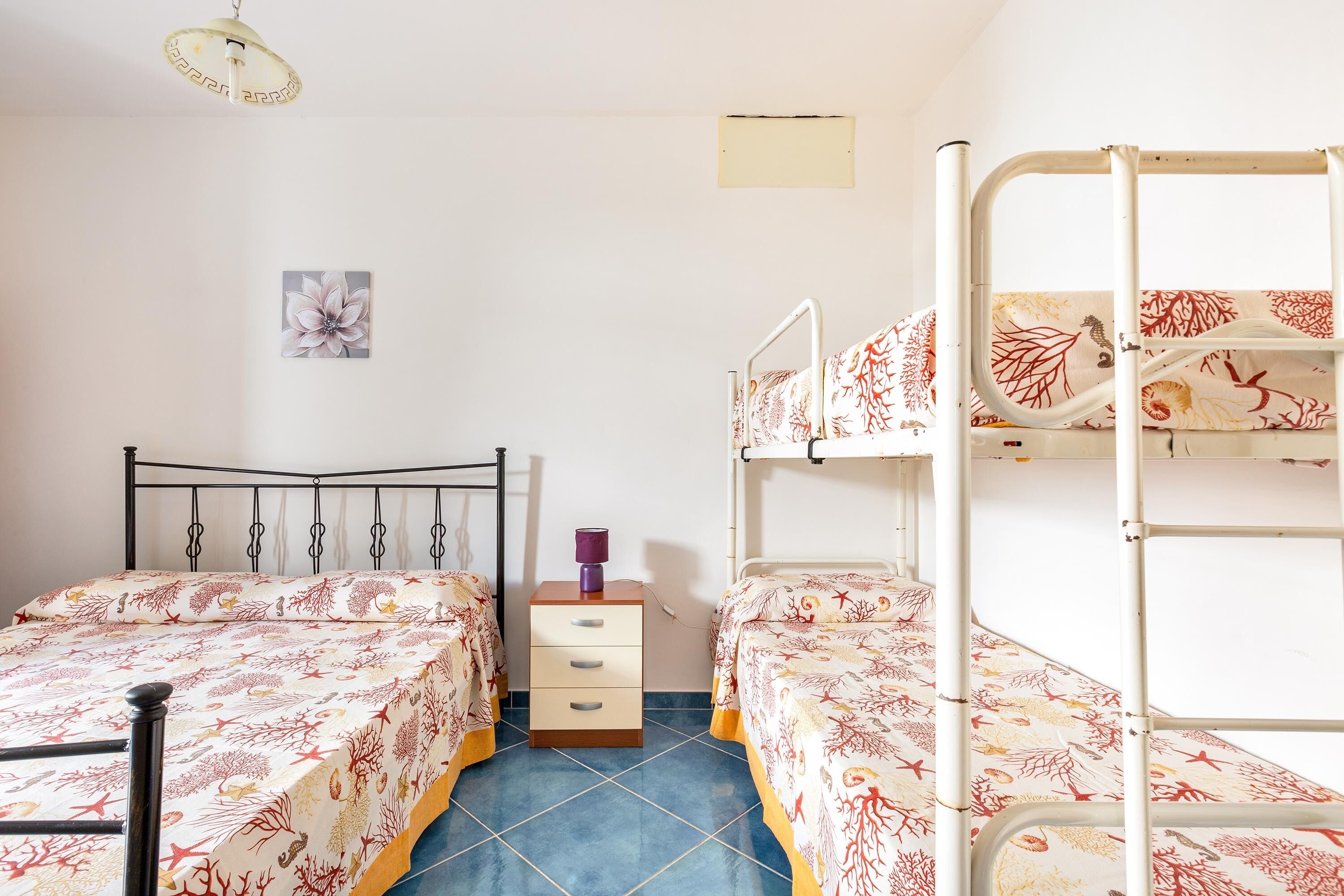 Quarto com beliche, mesa de cabeceira, luminária e prateleira na parede.