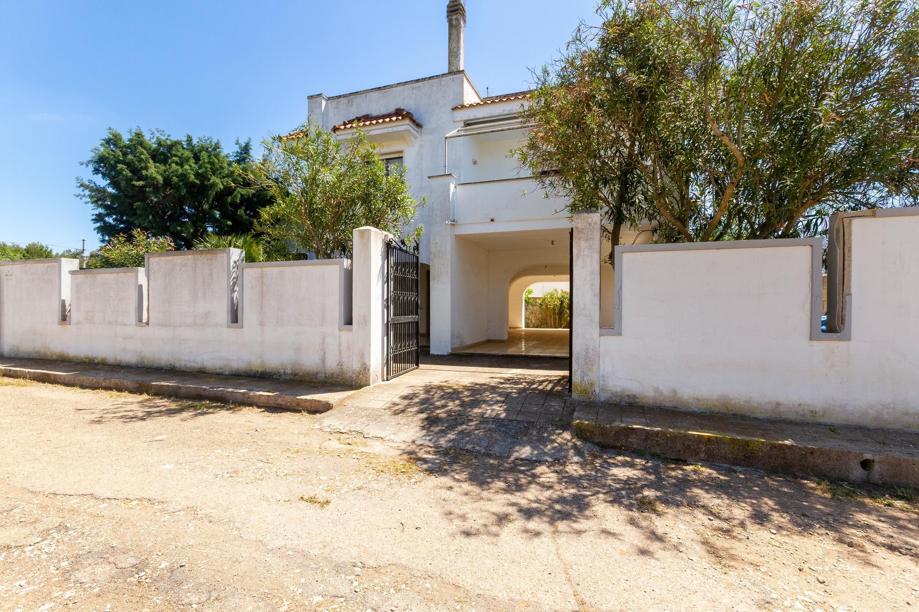 Um edifício branco com portão, chaminé e calçada de acesso pavimentada.
