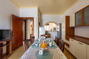 Uma área de refeições com uma mesa posta para quatro pessoas, uma televisão em um suporte e armários de madeira.