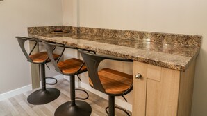 Uma cozinha com bancada de granito, três banquetas de bar e armários de madeira.