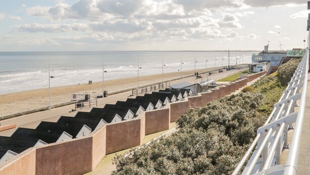 Um calçadão costeiro com praia, um muro marítimo e uma plataforma de observação.