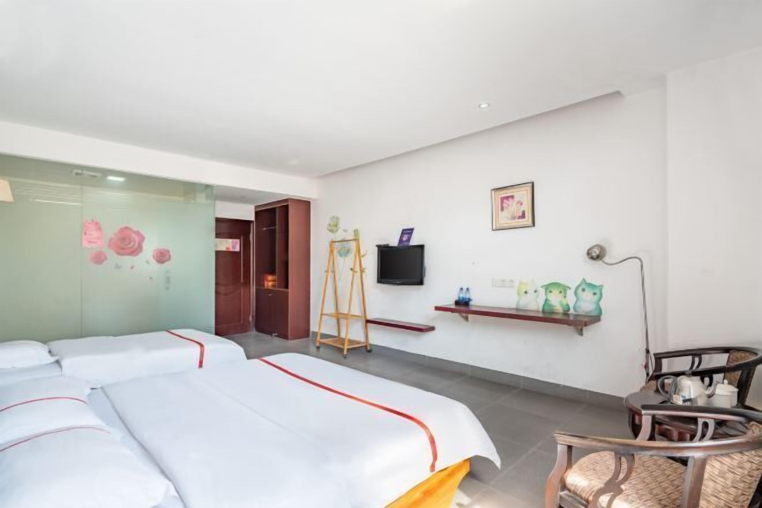 Quarto de hotel com uma cama, uma escrivaninha, uma cadeira, uma televisão e uma estante com objetos decorativos.