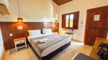 Um quarto com cama, mesas de cabeceira, teto de madeira, janela com persianas e uma porta.