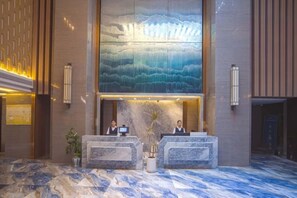 Uma área de recepção de hotel com uma grande exibição de arte digital, balcões de recepção e piso de mármore.