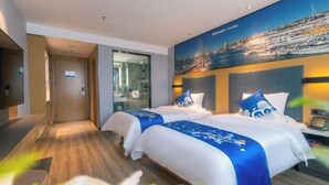 Quarto de hotel com duas camas, uma janela grande com vista para a paisagem urbana, televisão de tela plana e piso de madeira.