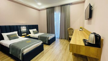 Quarto de hotel com duas camas, uma escrivaninha, uma cadeira, uma televisão e uma janela com cortinas.