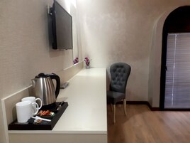 Quarto moderno com bancada branca, uma cadeira preta, uma pequena mesa com chaleira e xícaras, e uma TV fixada na parede.