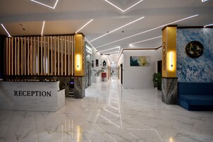 Uma área de recepção moderna com piso de mármore, balcão de atendimento identificado como “RECEPTION” e uma área de estar azul.