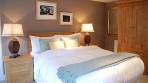 Cama bem arrumada com manta azul, duas luminárias de cabeceira e um guarda-roupa de madeira.