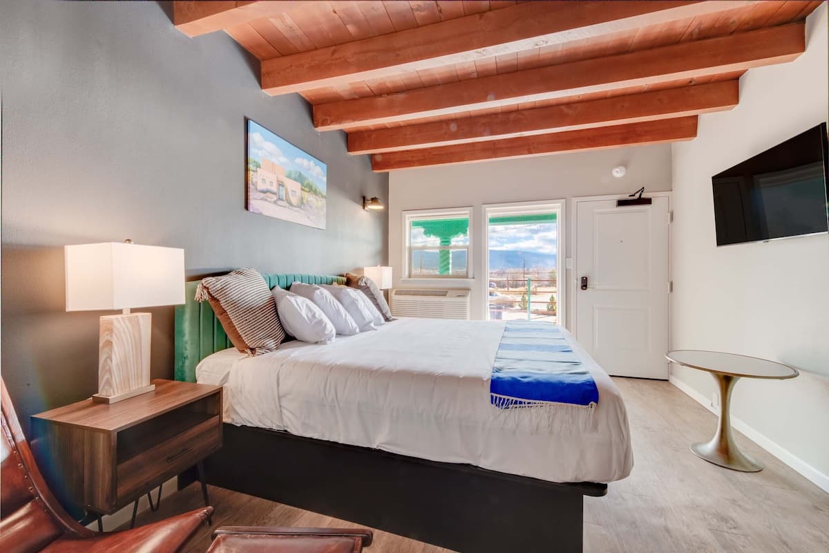 Quarto com cama, mesa de cabeceira, luminária, cadeira, televisão e janela com vista.