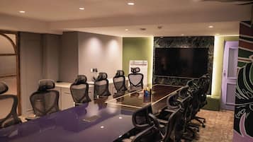 Uma sala de conferência com uma mesa comprida, diversas cadeiras, um quadro branco e uma televisão de tela plana grande na parede.