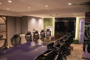 Uma sala de conferência com uma mesa comprida, diversas cadeiras, um quadro branco e uma televisão de tela plana grande na parede.