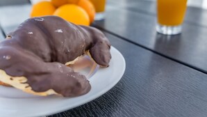 Um croissant em um prato branco com um copo de suco de laranja sobre uma mesa de madeira.