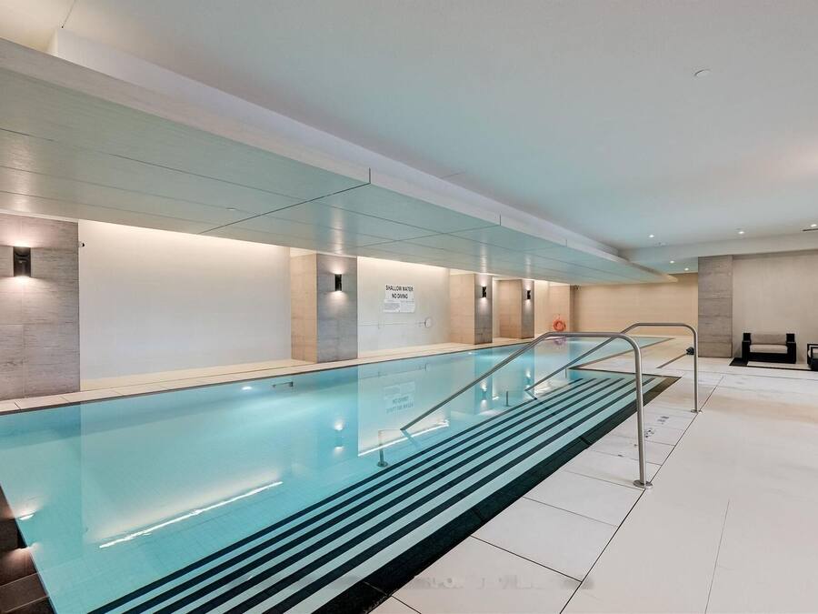 Piscina interior moderna com sinalização clara, barreira de vidro e piso revestido de azulejos.
