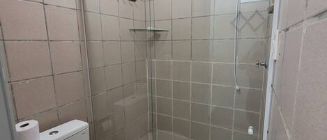 Uma casa de banho pequena com sanita, cabine de duche em vidro e uma toalha no assento da sanita.