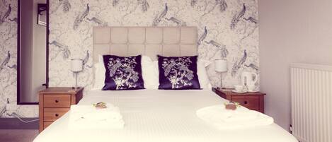 Quarto de hotel com uma cama grande, duas mesas de cabeceira, um espelho e um radiador.