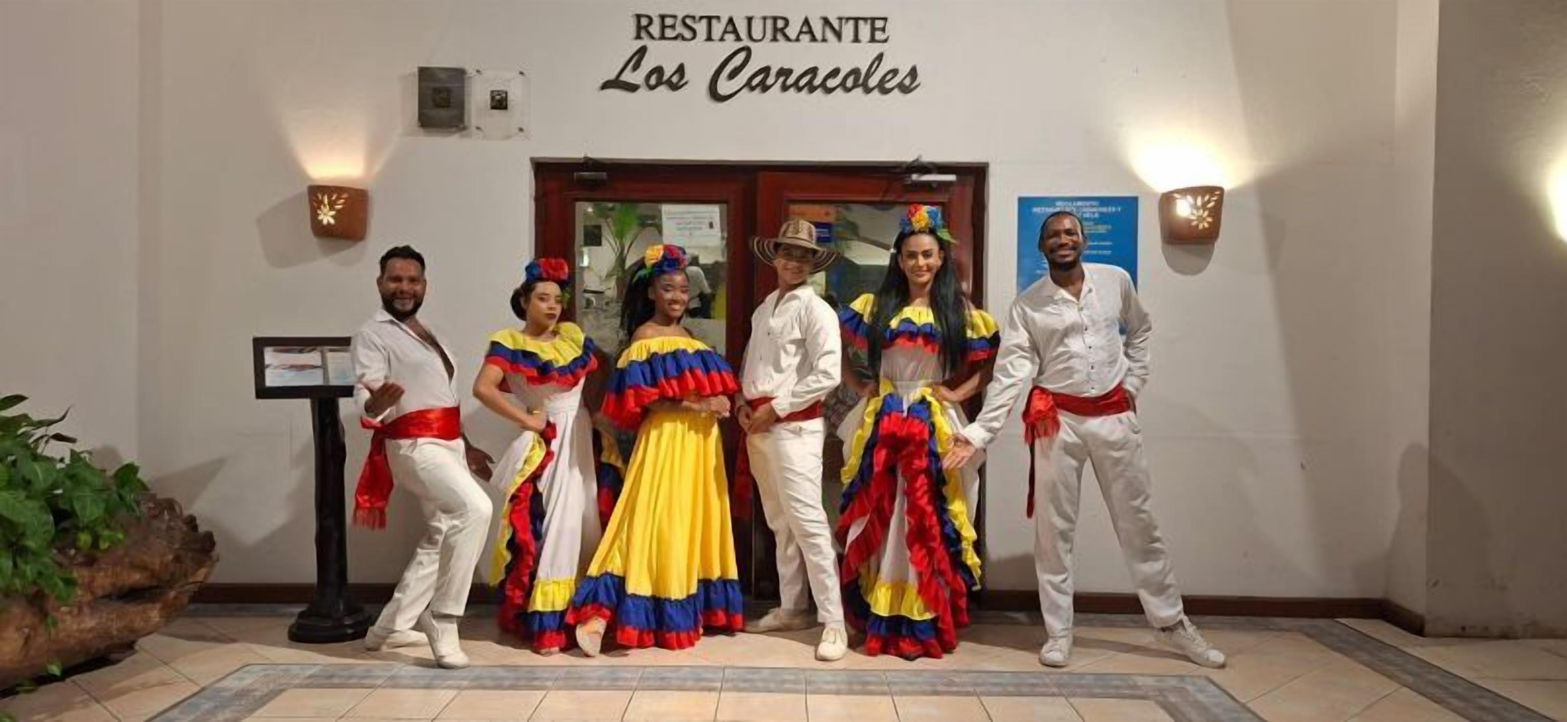 Um grupo de pessoas vestindo trajes típicos em frente a um restaurante chamado 'Los Caracoles'.