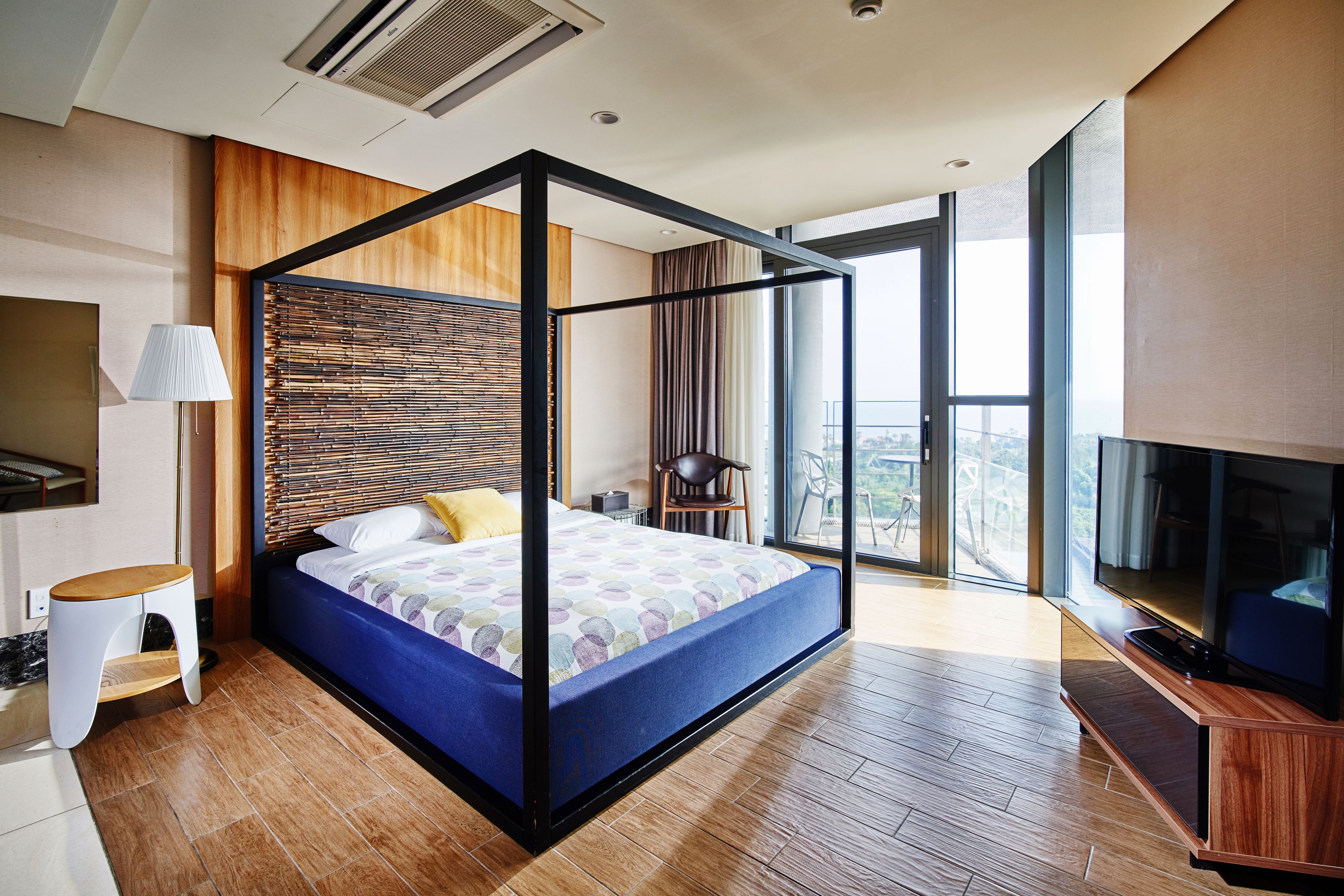 Quarto moderno com cama de dossel, televisão e grande janela com vista para a cidade.