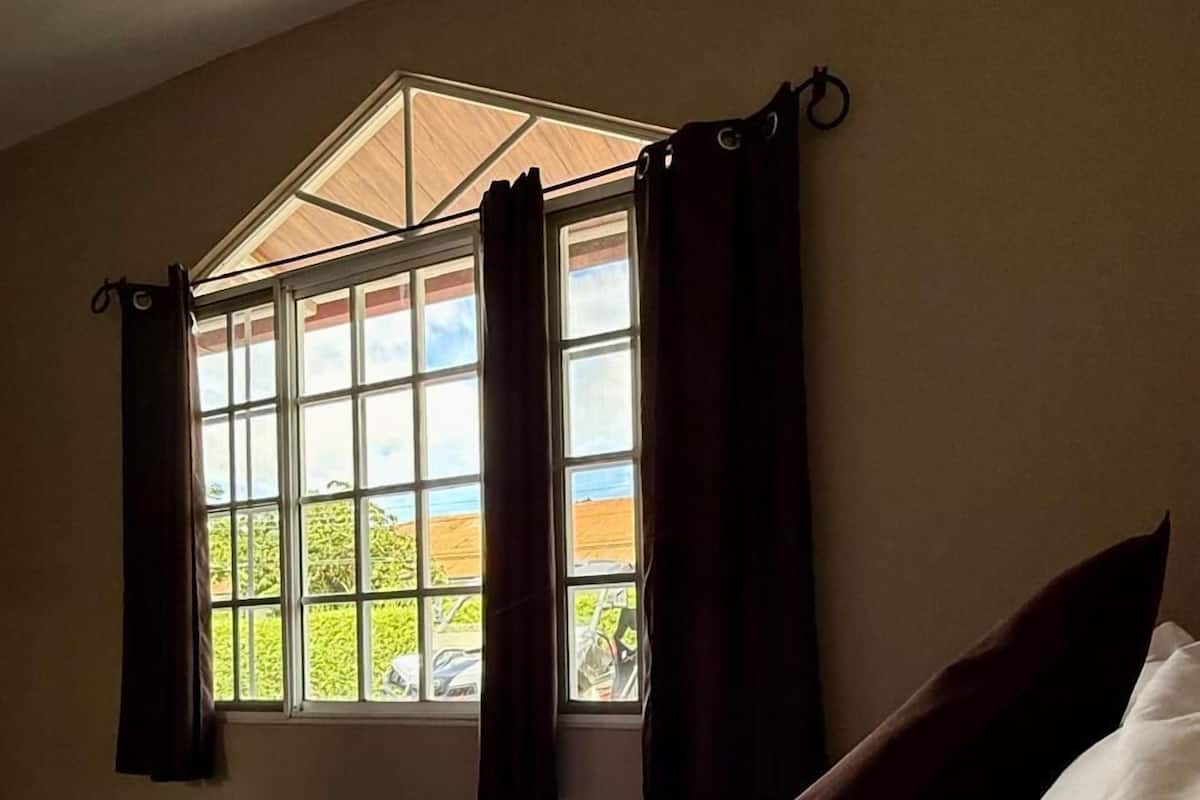 Quarto com uma cama grande, janela com cortinas e vista para o verde lá fora.