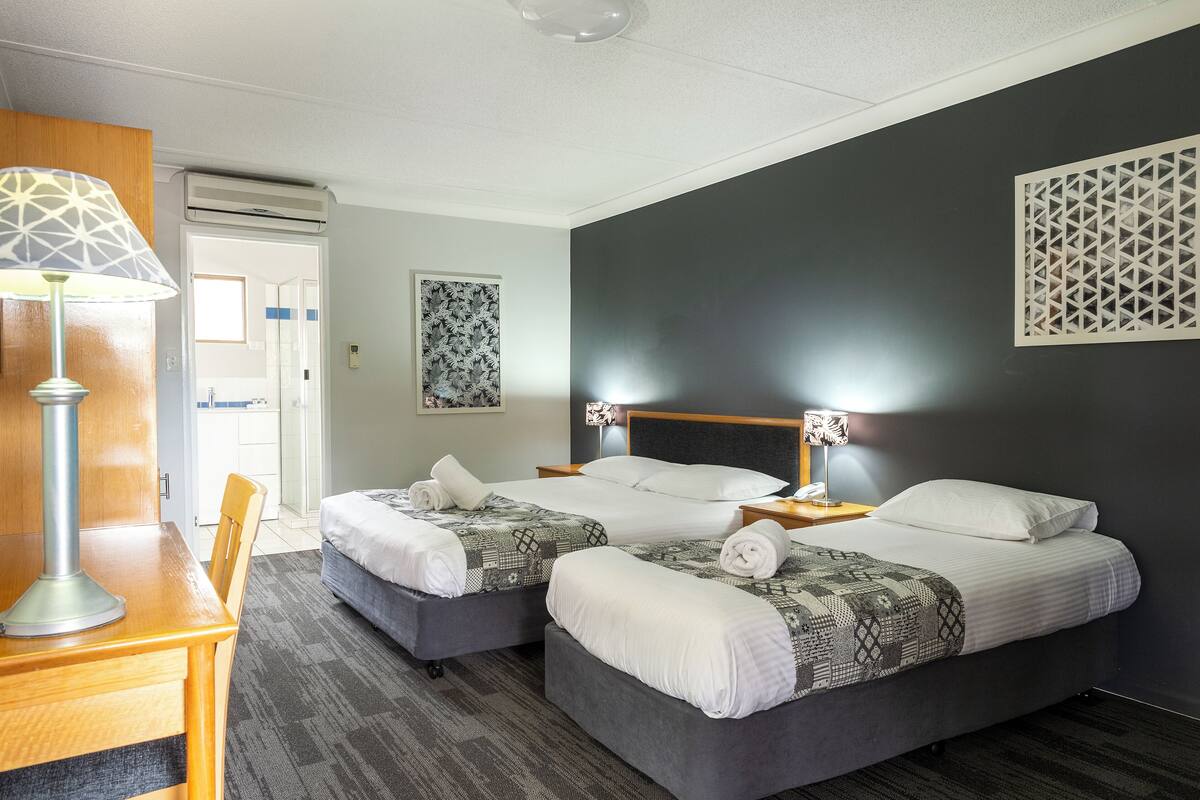 Quarto de hotel com duas camas, uma escrivaninha e uma luminária.