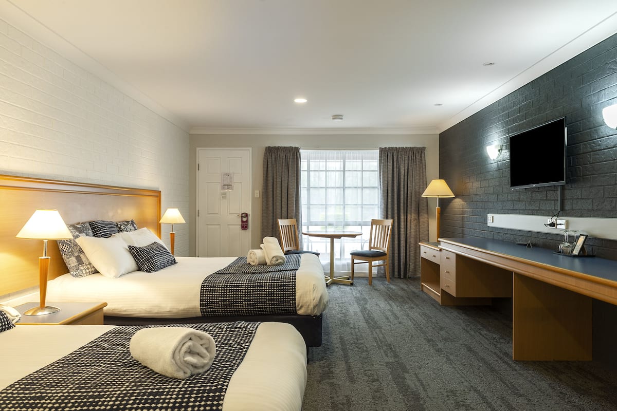 Quarto de hotel com duas camas, uma escrivaninha, uma cadeira, uma televisão e uma janela com cortinas.