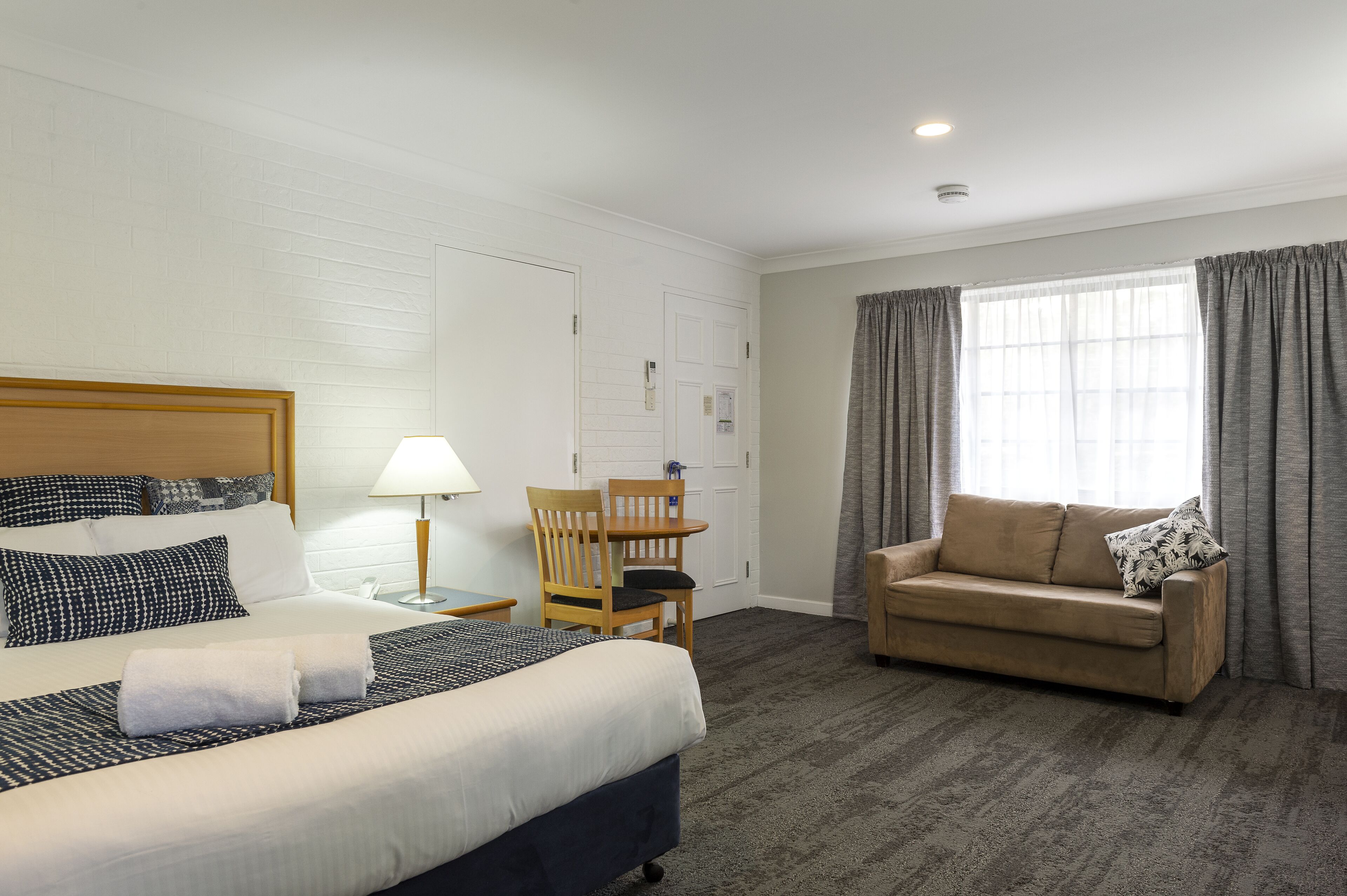 Quarto de hotel com uma cama, uma cadeira, um sofá e uma janela com cortinas.