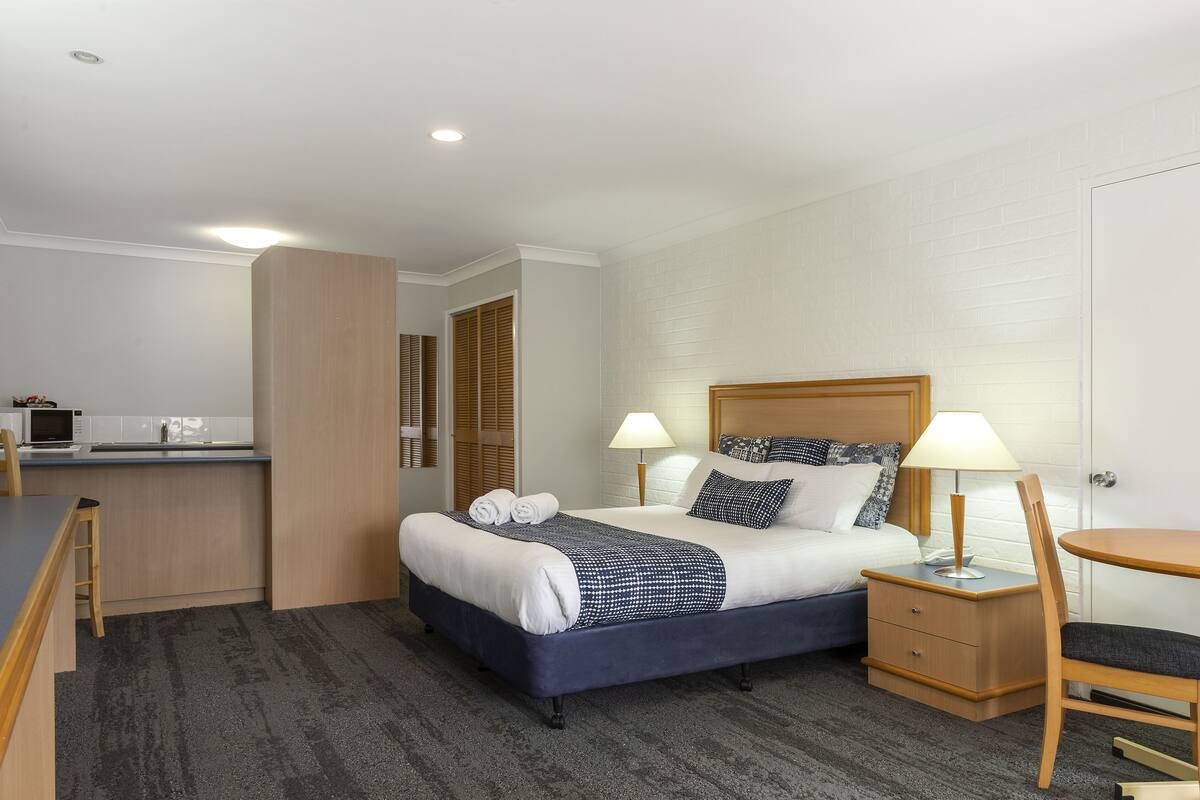 Quarto de hotel com cama, mesas de cabeceira, escrivaninha e uma cadeira.