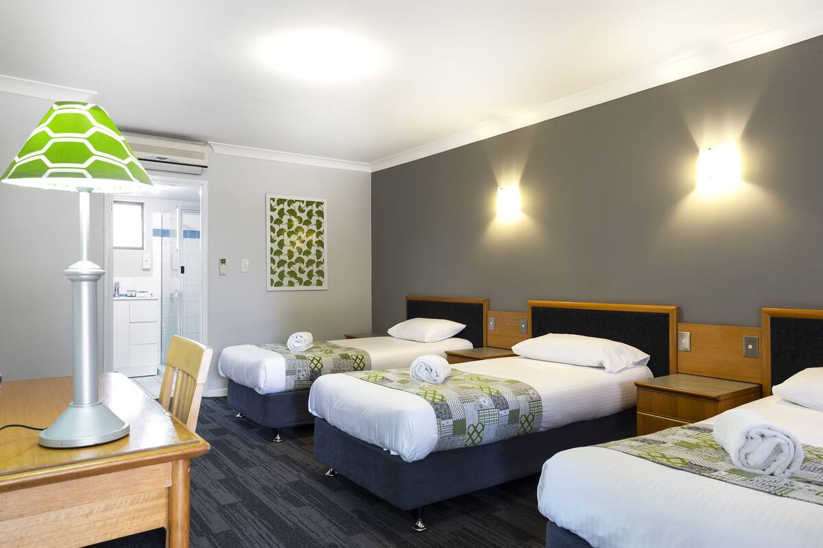 Quarto de hotel com duas camas de solteiro, uma escrivaninha com luminária e uma pequena mesa.