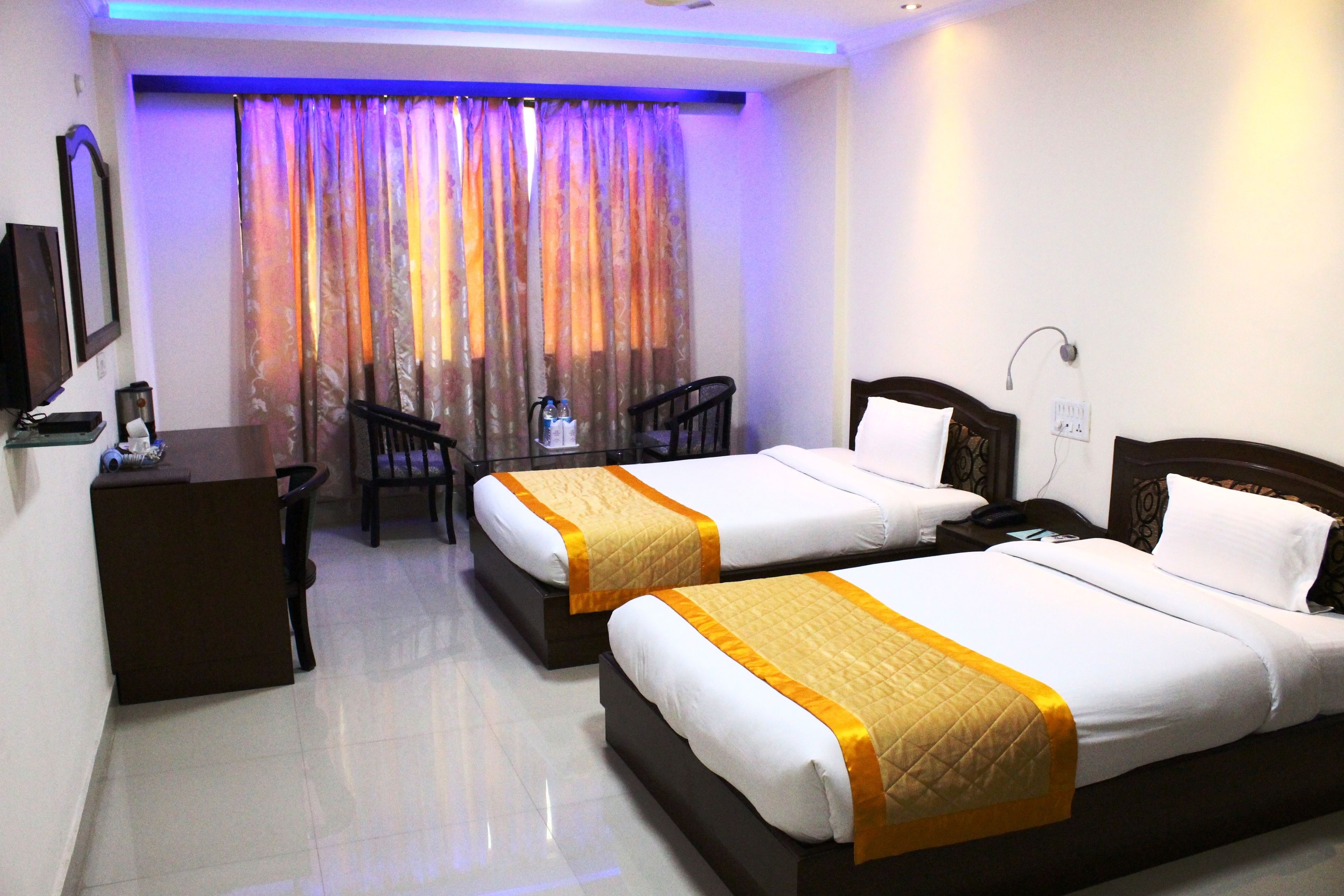 Quarto de hotel com duas camas, uma escrivaninha, uma cadeira e uma janela com cortinas.