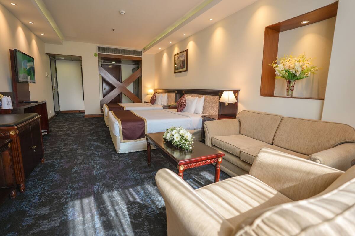 Quarto de hotel com duas camas, um sofá, uma mesa de centro e uma escrivaninha.