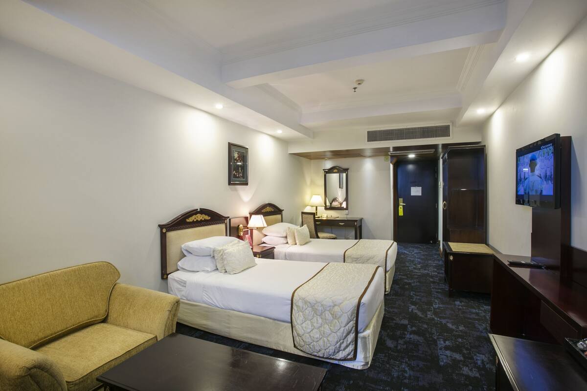 Quarto de hotel com duas camas, um sofá, uma escrivaninha, uma televisão e um espelho.