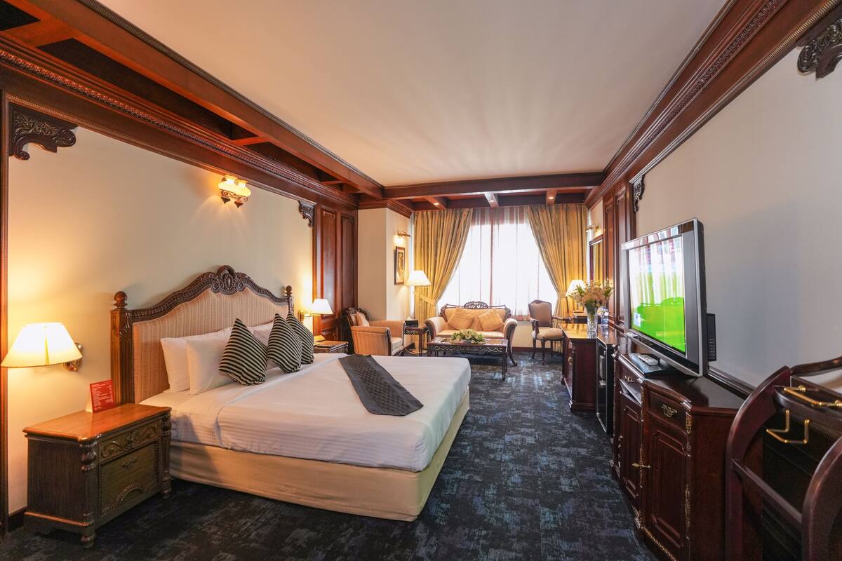 Quarto de hotel com uma cama grande, televisão, escrivaninha e sofá.