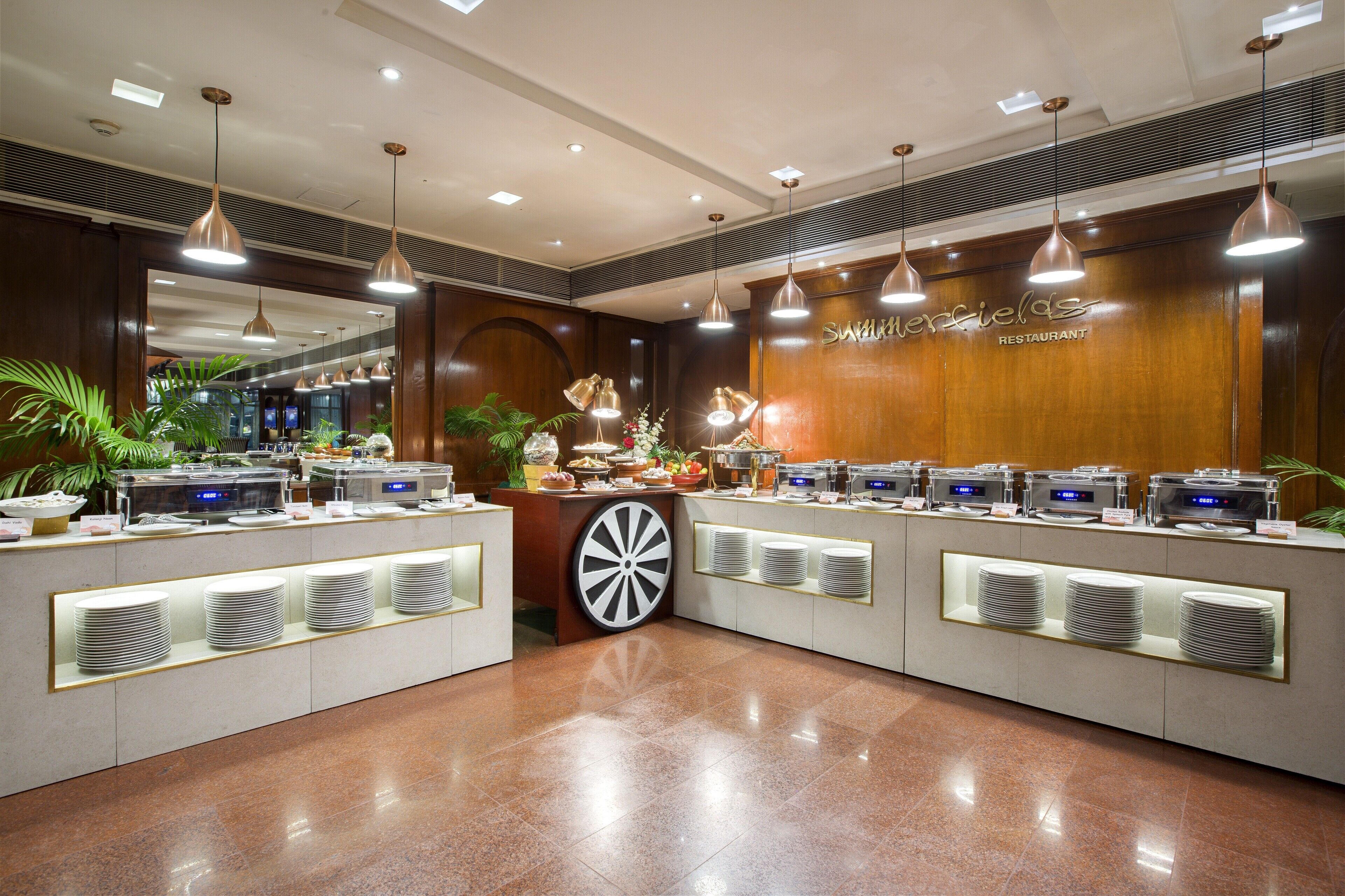 Uma área de buffet com várias estações de serviço, uma roda decorativa central e uma placa indicando 'Swimmerciel Restaurant'.