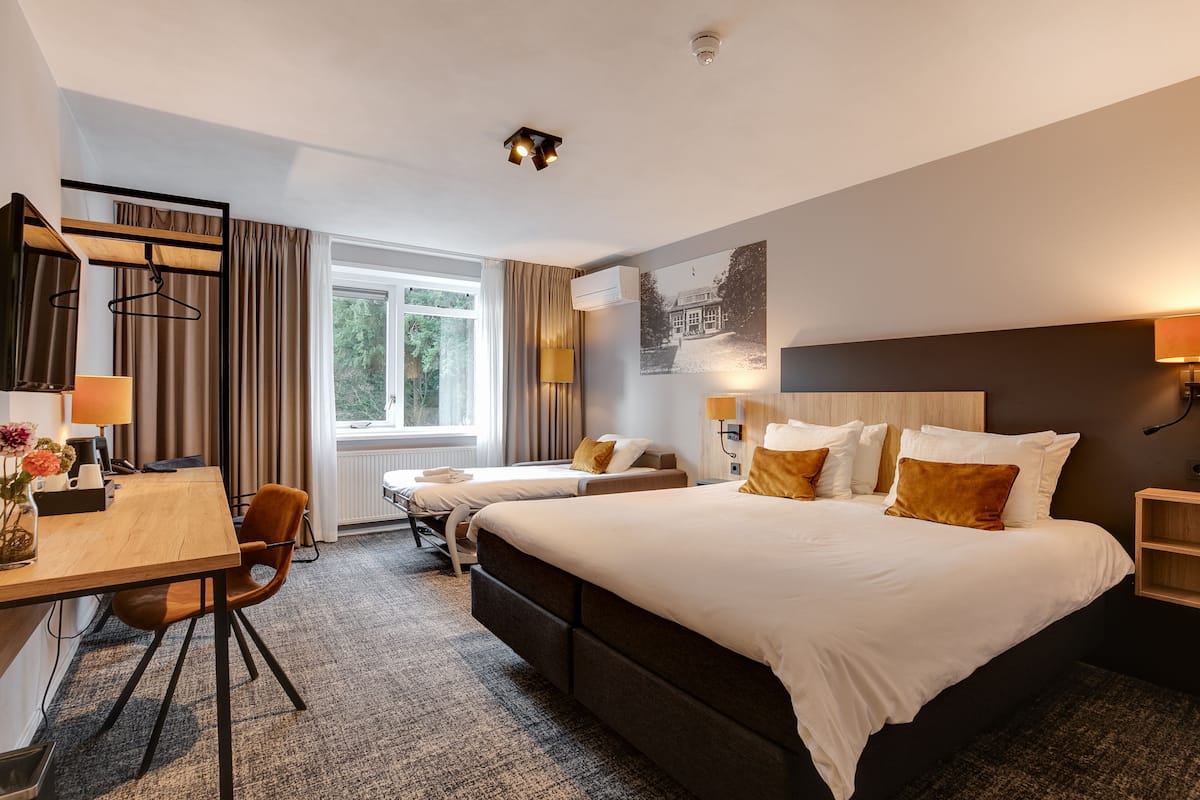 Quarto de hotel com uma cama grande, uma escrivaninha, uma cadeira e uma janela com cortinas.