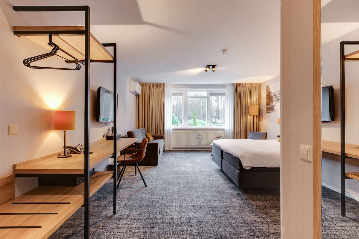 Quarto de hotel com cama, escrivaninha, cadeira, televisão e janela com cortinas.