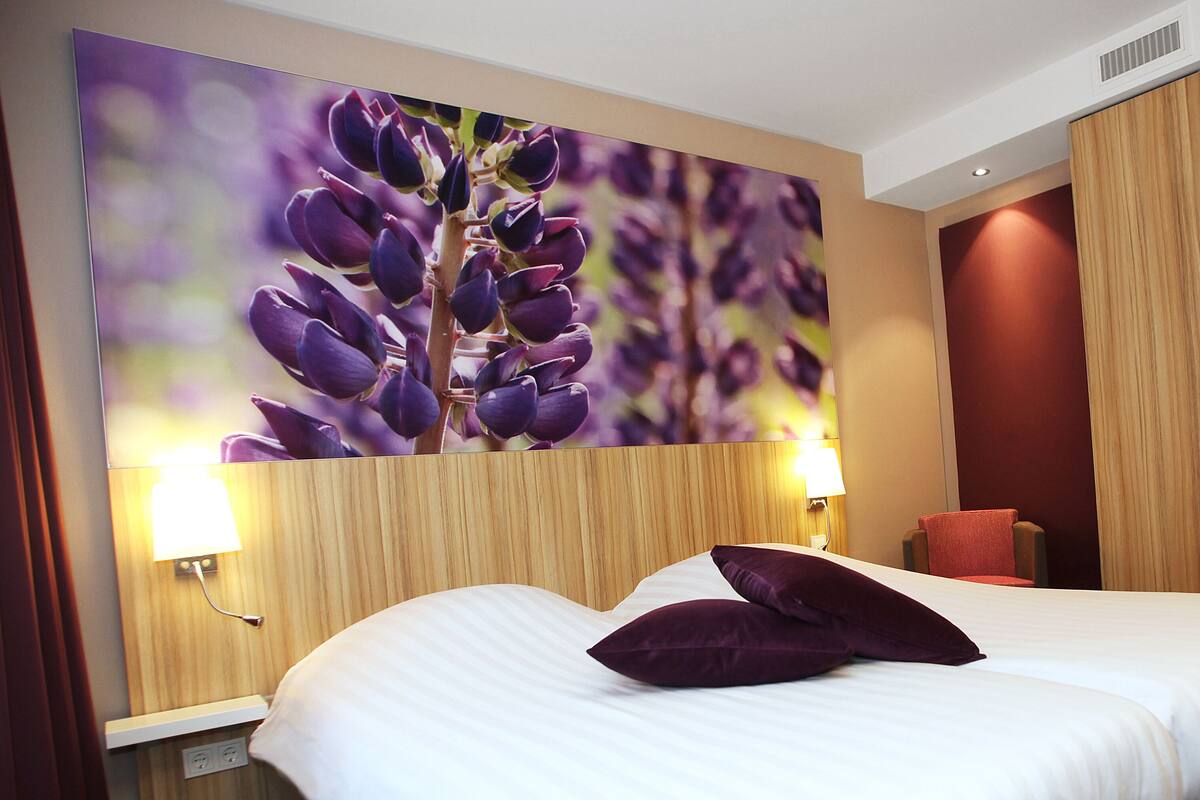 Quarto de hotel com uma cama grande, uma cadeira vermelha, uma cabeceira de madeira e uma luminária na parede.