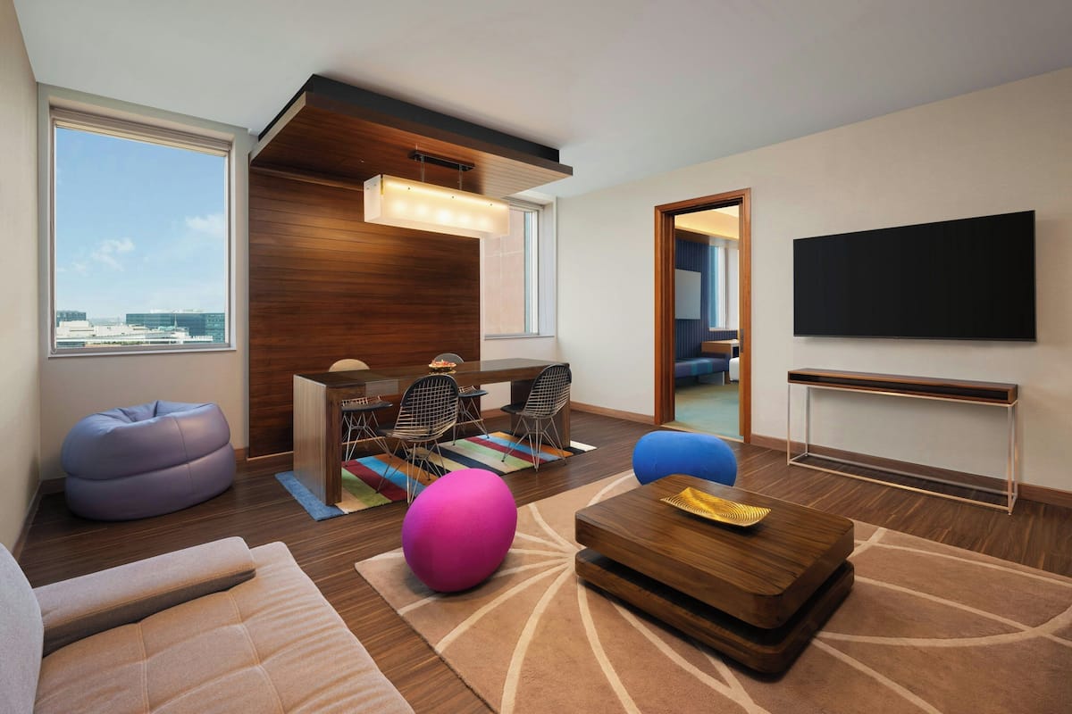 Uma sala de estar moderna com um sofá, poltronas de saco e uma mesa de centro, e uma TV fixada na parede.