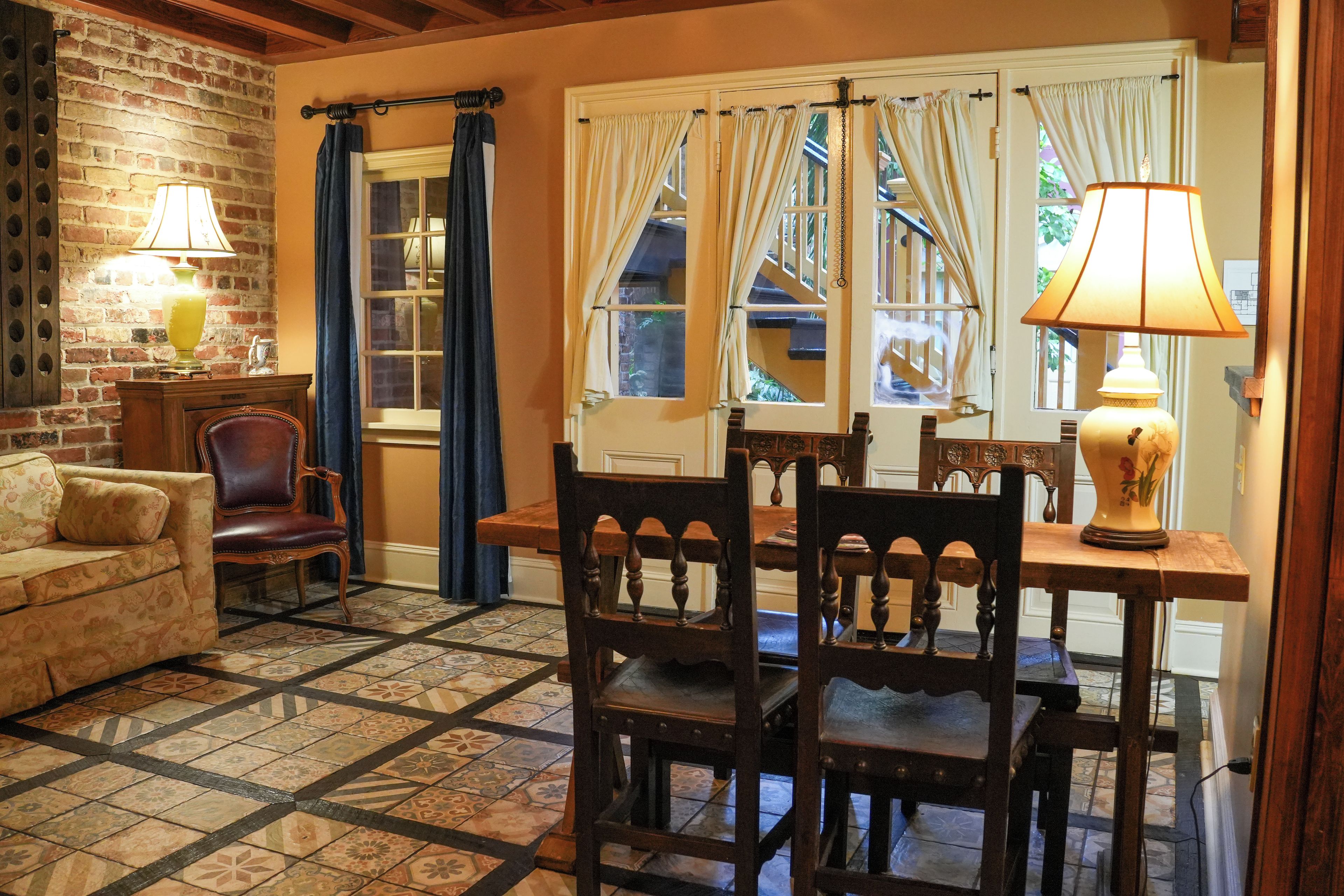 Quarto aconchegante com parede de tijolos, mesa de madeira com cadeiras, sofá e duas luminárias.