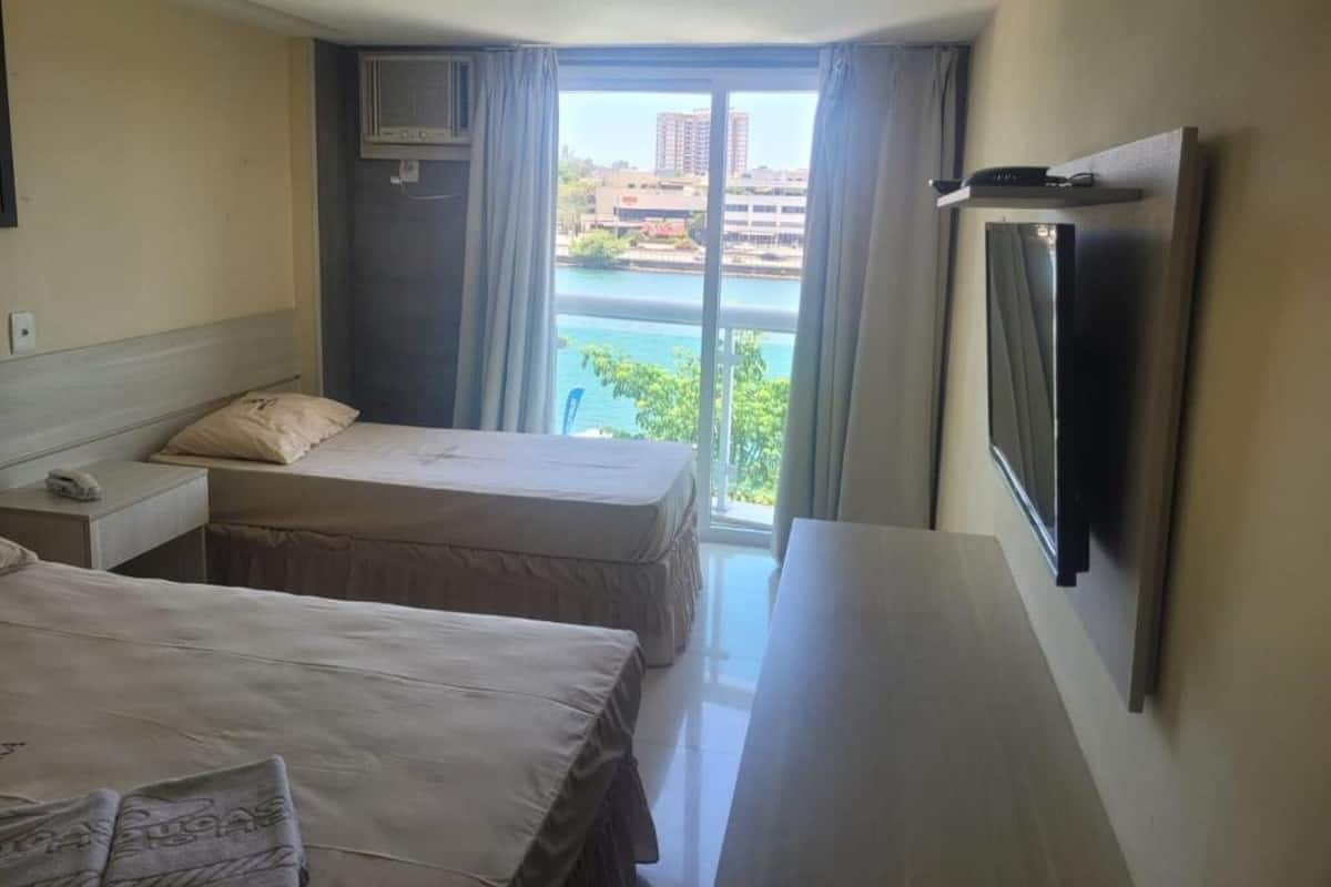 Quarto de hotel com duas camas, televisão e vista para a água.