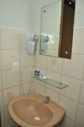 Uma casa de banho com uma pia bege, um espelho e dois secadores de cabelo fixados na parede.