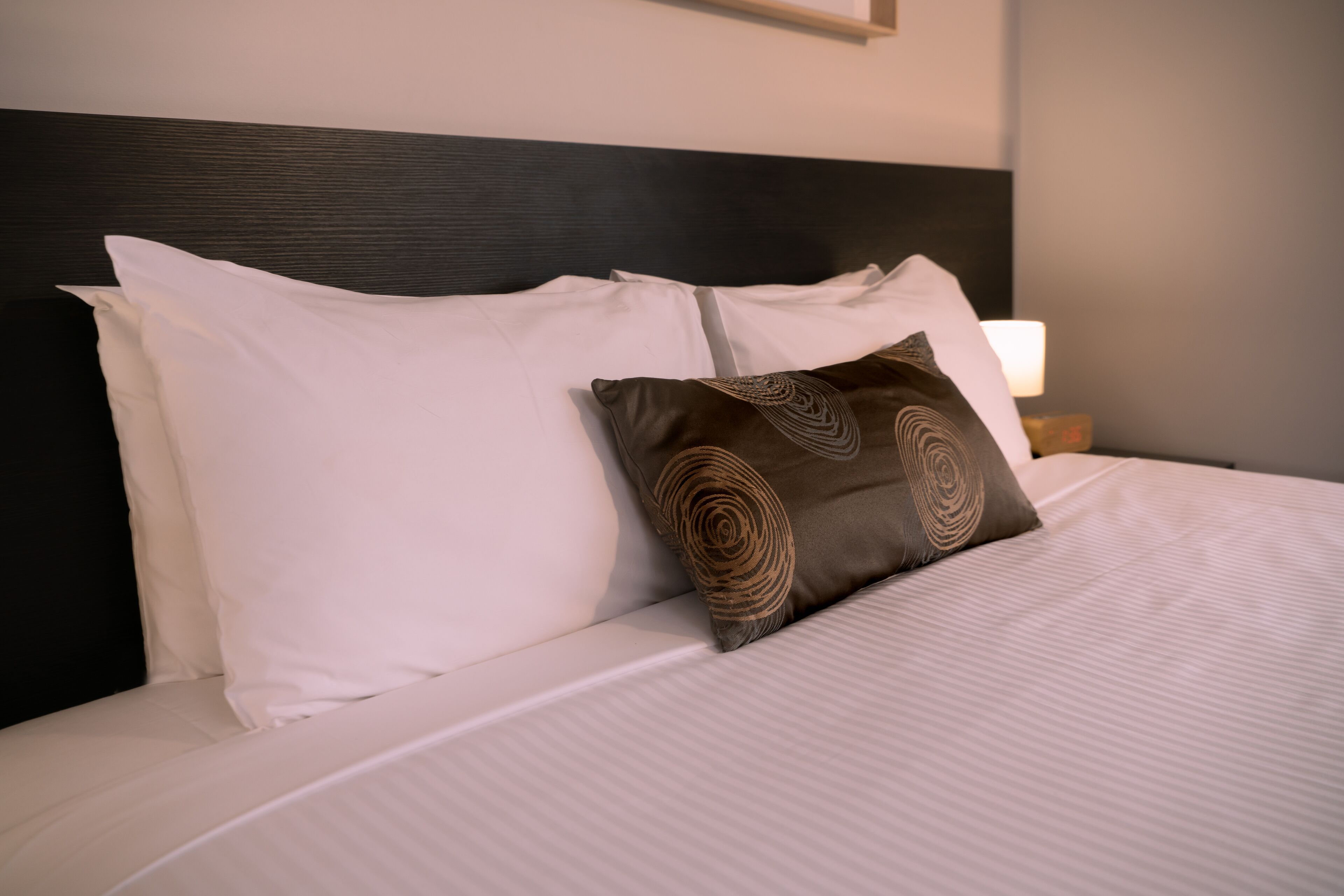 Cama bem arrumada com lençóis brancos e almofada decorativa com círculos concêntricos.