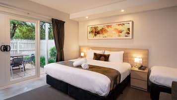 Quarto de hotel com uma cama grande, mesa de cabeceira com abajur, uma cadeira e uma porta de vidro deslizante que dá para uma área externa com mesa e cadeiras.
