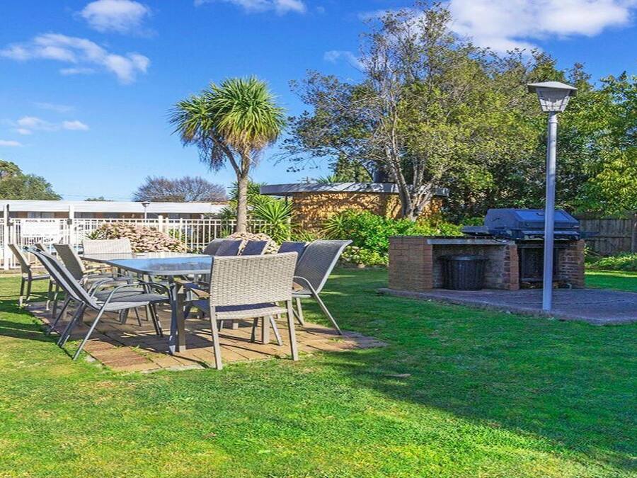 Um quintal com mesa e cadeiras de pátio, churrasqueira e uma área cercada com piscina.