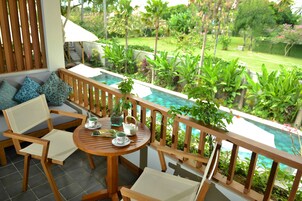 Um deck de madeira com mesa e cadeiras, com vista para uma piscina e um jardim exuberante.