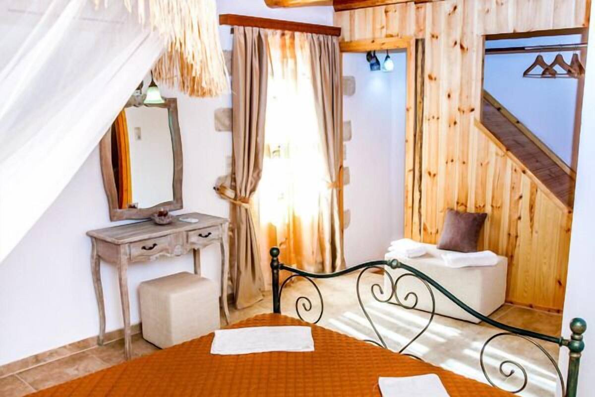 Quarto com cama, cômoda de madeira, espelho e janela com cortinas.
