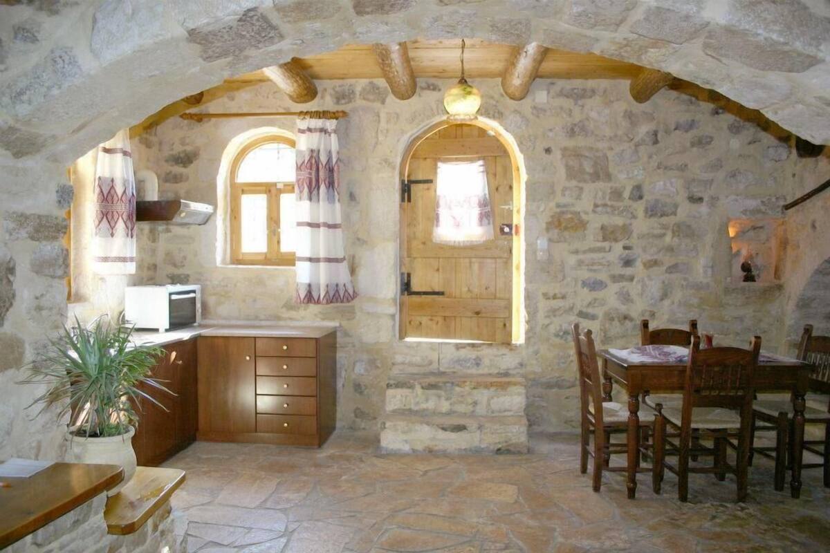 Cozinha rústica de pedra com armários de madeira, uma mesa de jantar e cadeiras.