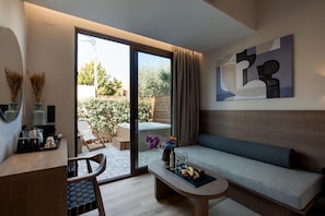 Uma sala de estar moderna com um sofá, mesa de centro e uma área de jantar com cadeiras. Há uma porta de vidro deslizante que dá para um pátio externo com hidromassagem e vegetação.